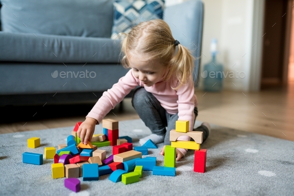 girl playing with colorful wooden blocks on the floor at home ...