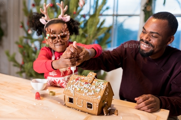 African american father and daughter decorating gingerbread house ...