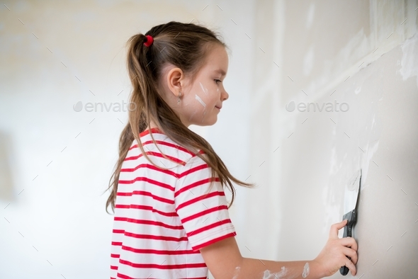 Child girl with trowel plastering a wall during house renovation ...