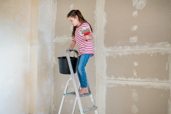 Child girl with trowel plastering a wall during house renovation ...