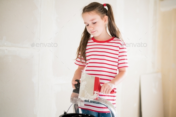Child girl with trowel plastering a wall during house renovation ...