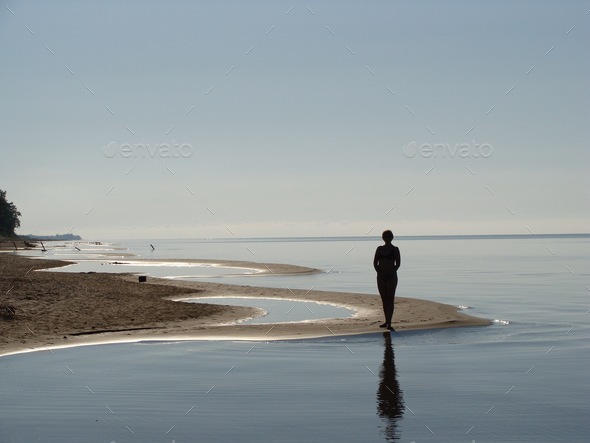 Seashore with a single person silhouette at the water edge, water is ...