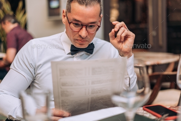 Man looking at menu in restaurant wearing glasses and bow tie formal ...