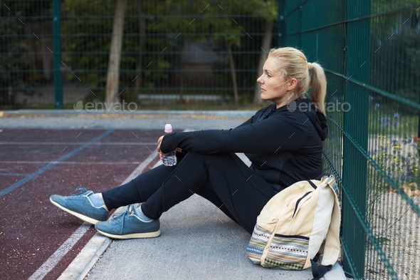 Young overweight active woman sitting on the street workout place after ...