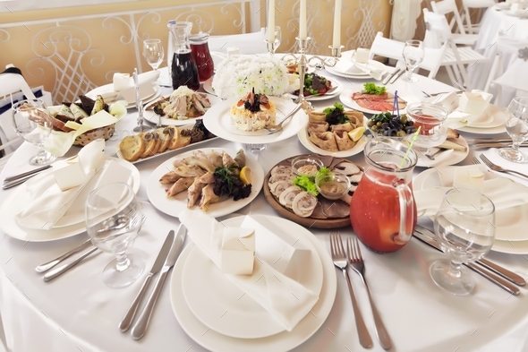 Banquet table with drinks, appetizers and salads on white tablecloth in ...
