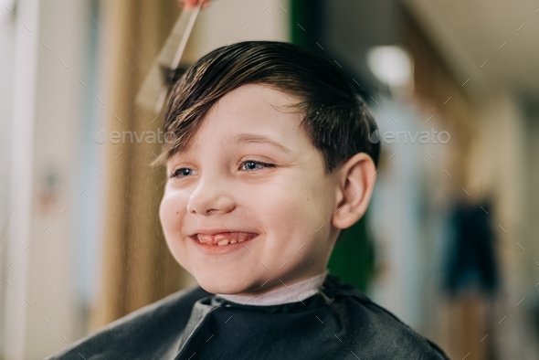 Little kid boy in the barbershop or hairdressing saloon. Barber is ...