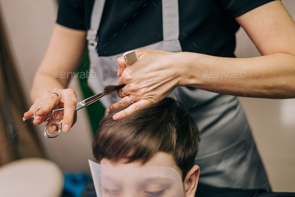 Little kid boy in the barbershop or hairdressing saloon. Barber is ...