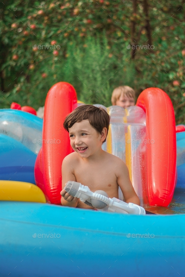 Little kid boy playing water bluster in the blown swimming pool at ...