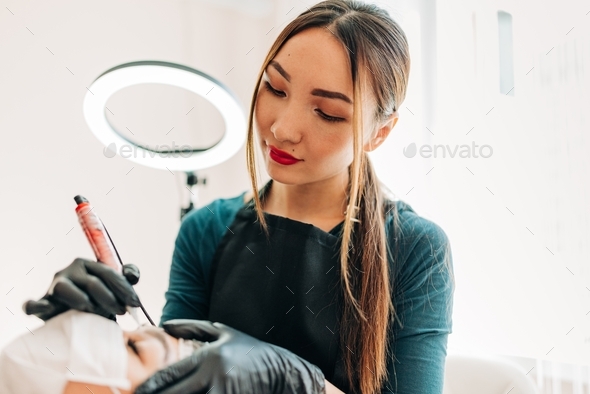 Cosmetologist doing permanent makeup tattooing for brows in her office ...