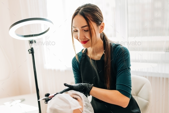 Cosmetologist doing permanent makeup tattooing for brows in her office ...