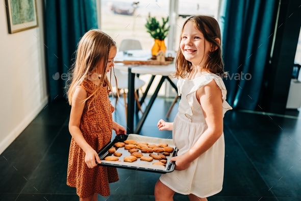 Kids girls cooked cookies and bringing them to the table on the kitchen ...