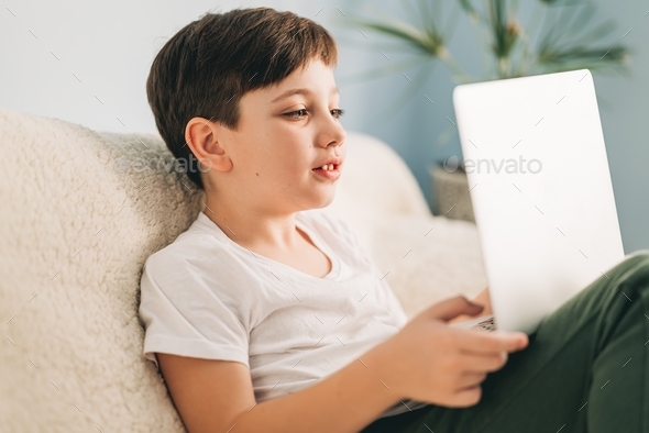 Little boy kid schoolboy sitting on the sofa couch working using laptop ...