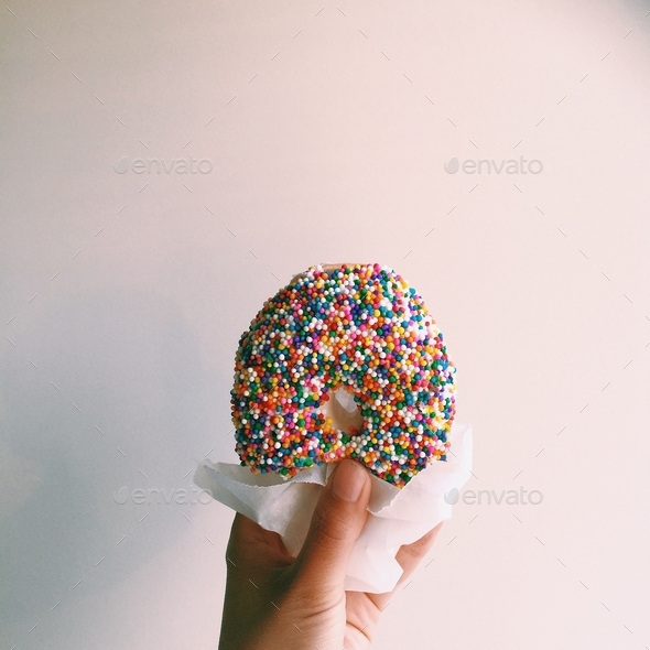 Holding a sprinkle covered donut up against a simple white wall. Stock ...