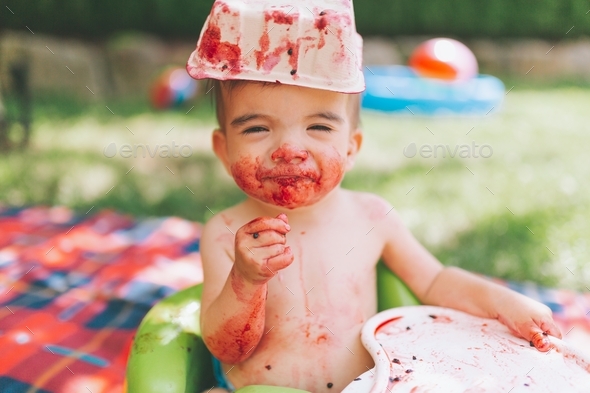 A messy baby eating berries, with juice all over his face in the summer ...