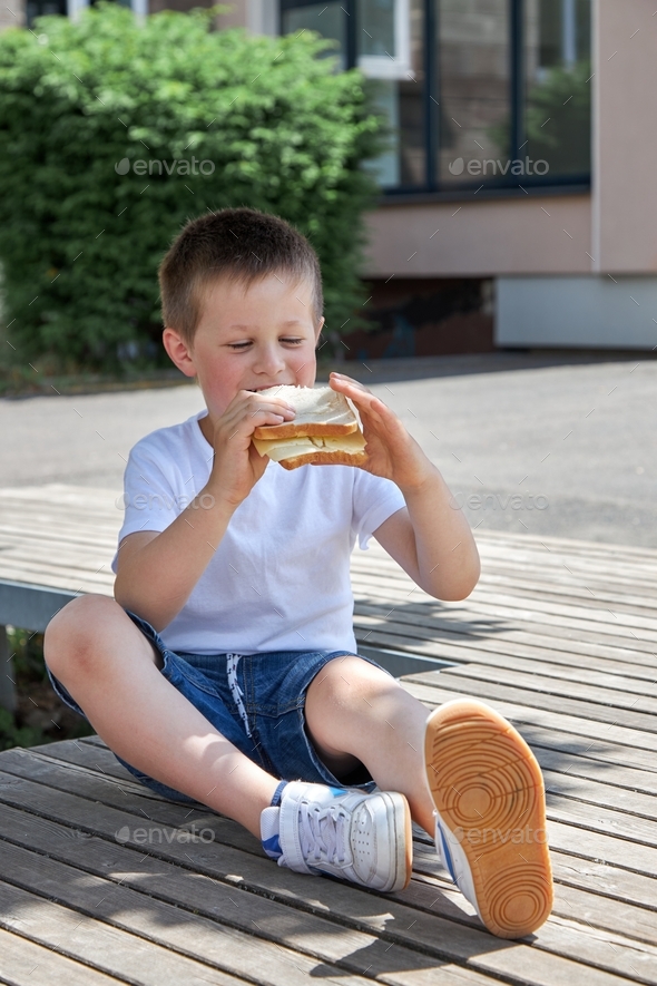 Boy eats a sandwich in the schoolyard during recess Stock Photo by elmedoks