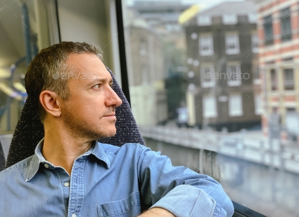 Middle aged man is traveling in a train. Looking through the window ...