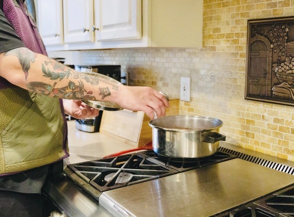 Adult male adding salt to a pot of simmering food cooking on the stove ...