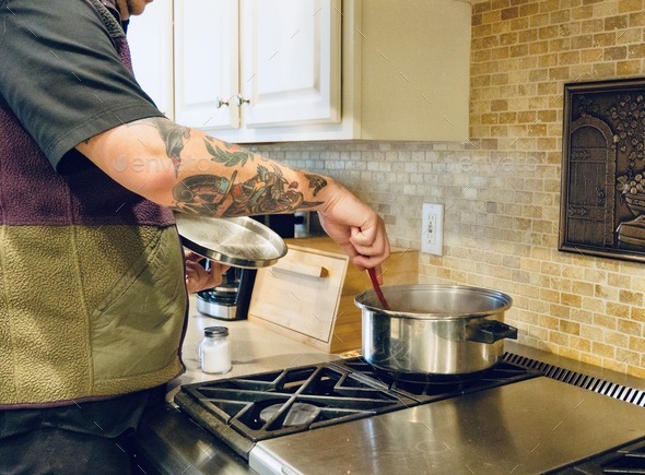 Adult male with tattooed arm using big spoon to stir simmering beans in ...