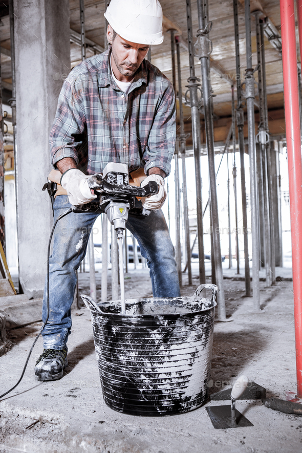A mason in a building under construction prepares cement in a bucket ...