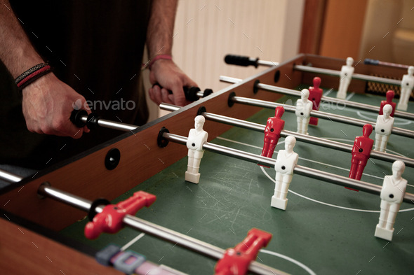 Photograph of a man's hands playing a foosball table with red and white ...