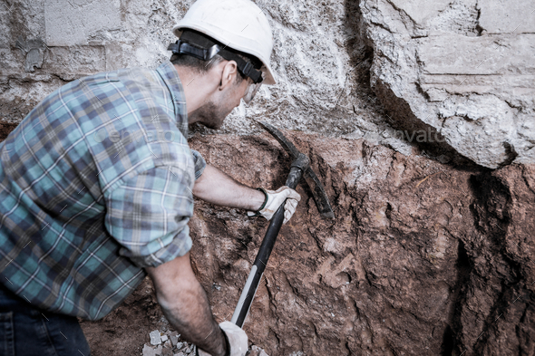 A worker dressed in his safety clothing opens a hole in the wall with a ...