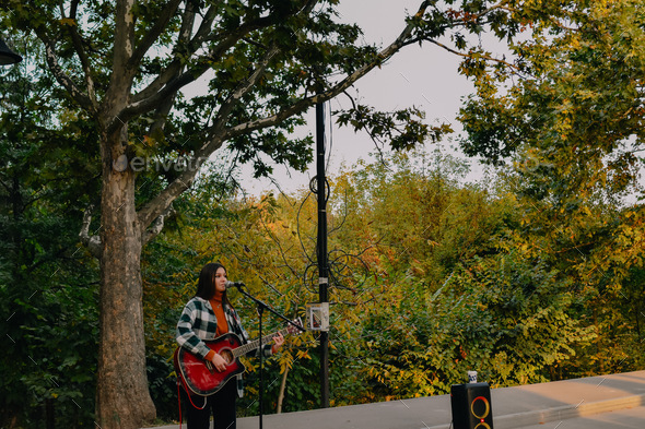 Singing girl playing on guitar in the park Stock Photo by VictoriaColin