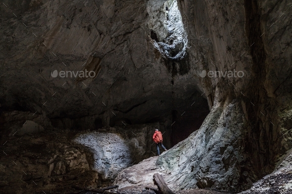 Man inside a cave, admiring the imposing walls and carstic formations ...