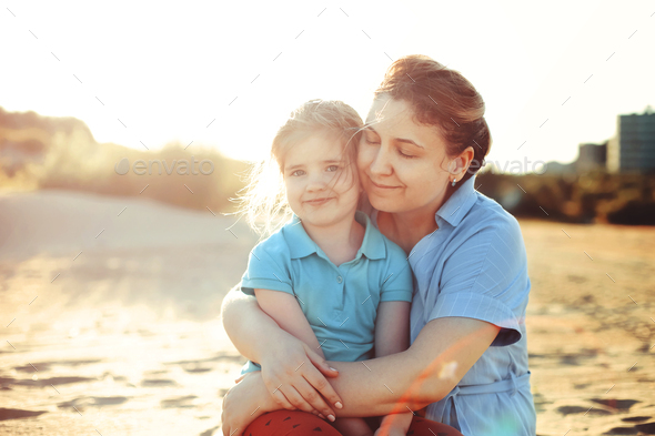 Young loving mother with smiling daughter hugging her little daughter on sunny beach Stock Photo ...