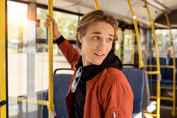 portrait of smiling man holding bus handle while riding in public ...