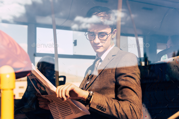 side view of man with newspaper in hands checking time while riding in ...