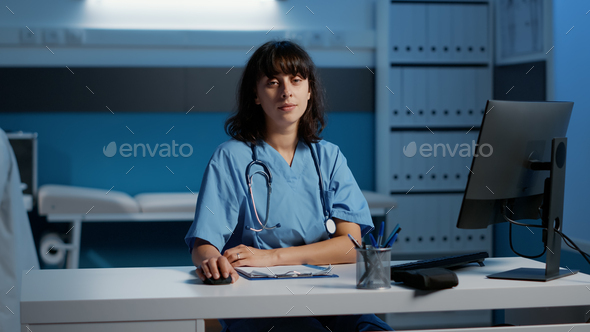 General practitioner nurse sitting at desk working over hours at ...