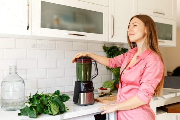 Cheerful young woman making smoothie using blender in the kitchen Stock ...