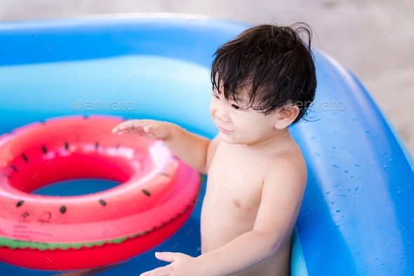 Side view. Asian boy stands in a blue rubble pool with a red rubber ...