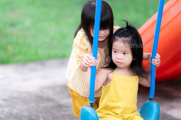 The sisters taught the sisters to play swings. Two child girl sisters ...