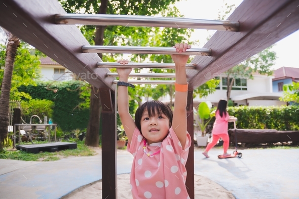 Asian girls are playing on playground with trapeze. Active child hangs ...