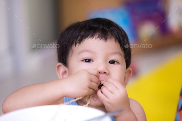 Preschool Asian boy is using hands to pick up instant noodles in mouth ...