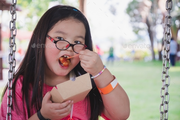 Cute Asian girl eating snacks from paper plate. Child sit on swing ...