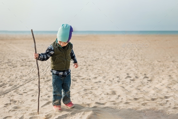 child explores the sand on the sea beach with a big stick Stock Photo ...
