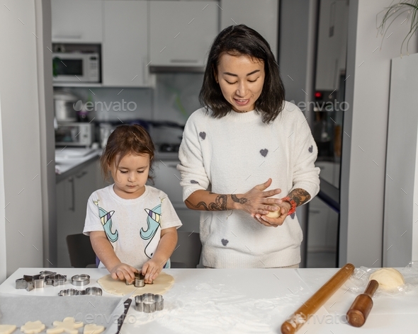 a little girl and her mother cook shortbread cookies using curly tin ...