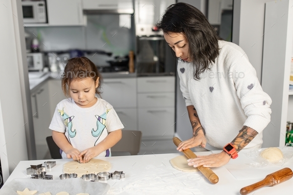 a little girl and her mother cook shortbread cookies using curly tin ...