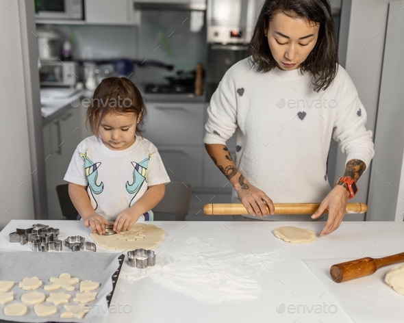 a little girl and her mother cook shortbread cookies using curly tin ...