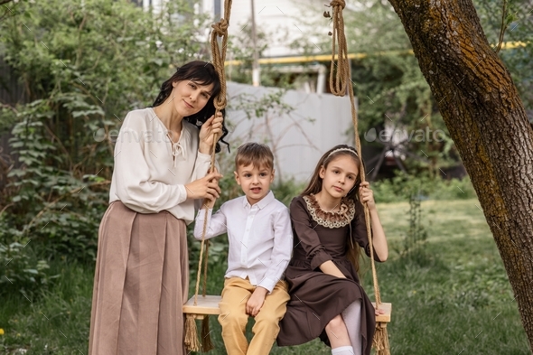 mom with two children sitting on a rope swing in the yard of a country ...