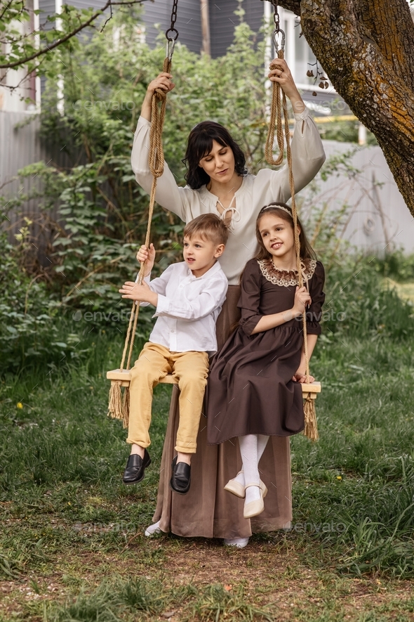 mom hugs two children sitting on a rope swing in the courtyard of a ...