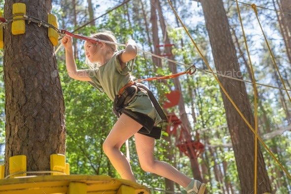 cute girl in forest adventure park, climb on high rope trail. Stock ...