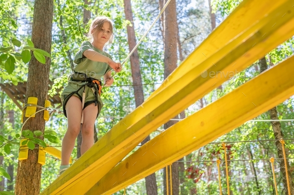 cute girl in forest adventure park, climb on high rope trail. Stock ...