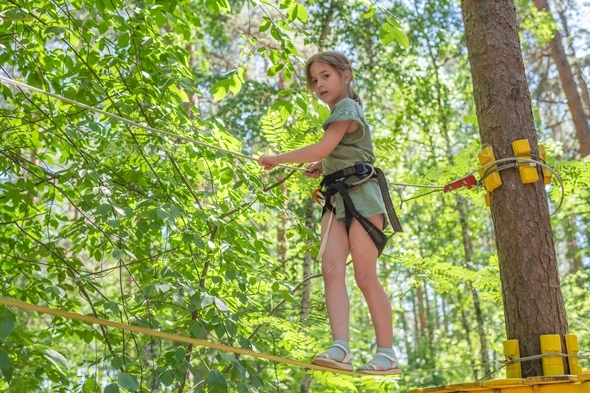 cute girl in forest adventure park, climb on high rope trail. Stock ...