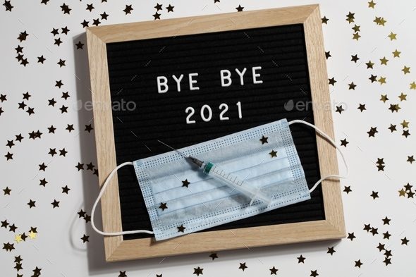 black letter board with text BYE BYE 2021 with small stars, syringe and ...