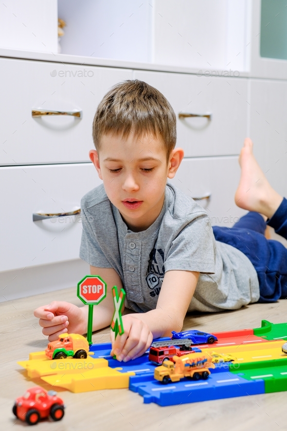 The boy plays with bright multi-colored cars on a plastic auto rally ...