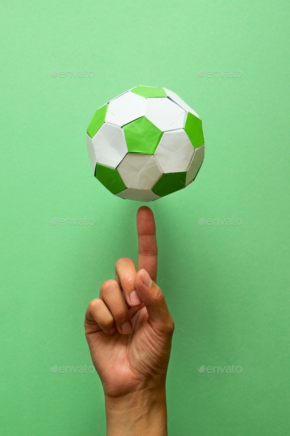 Hand spinning paper soccer ball on green background. Origami. Paper ...