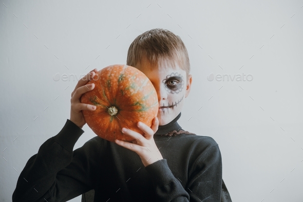 Scary boy celebrating Halloween, holds pumpkins, terrifying skull face ...